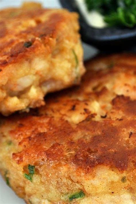 Two Crab Cakes On A White Plate With Some Sauce And Parsley In The