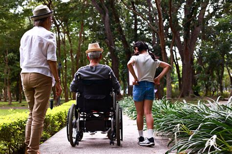 노부부와 어린 소녀가 정원 공원을 걷고 있고 휠체어를 탄 할아버지가 공원을 가로질러 걷고 있다 가족에 대한 스톡 사진 및 기타 이미지 Istock