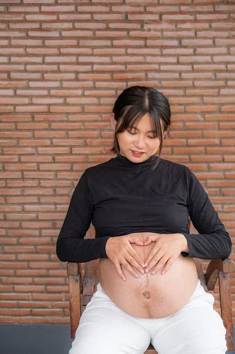 드레스를 입은 엄마 임산부는 붉은 벽돌 배경에 배꼽에 손을 얹고 사랑으로 아기의 탄생을 기다리고 있다 가정의 방에 대한 스톡 사진 및 기타 이미지 Istock