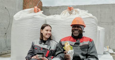 건설 현장의 쾌활한 이문화 노동자들은 콘크리트 또는 기타 건축 자재가 있는 자루에 대해 점심을 먹고 휴식 시간에 수다를 떨고 있습니다 사진 Unsplash의 러시아 이미지