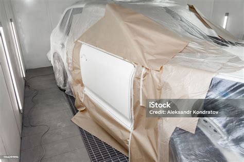 대형 흰색 차는 밝은 조명이 있는 차량의 차체 수리를 위한 워크샵에서 사고 후 페인팅 및 수리 중 스플래시를 방지 하기 위해 종이 및 접착 테이프로 완전히 덮여 있습니다