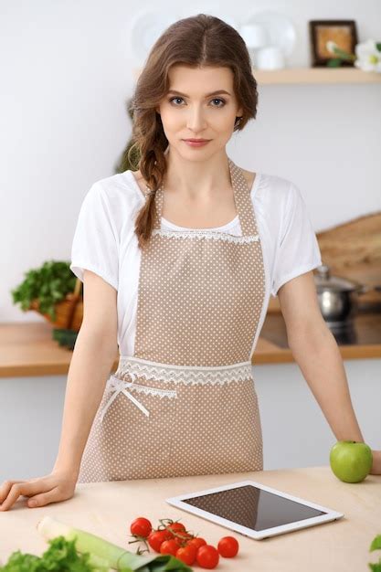 หญิงสาวผมสีน้ำตาลกำลังทำอาหารและชิมสลัดสดในครัว แม่บ้านถือช้อนไม้ไว้ในมือ แนวคิดเรื่องอาหารและ