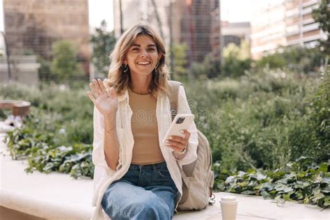 Smiling Young Caucasian Girl Waving At Camera Holding Smartphone