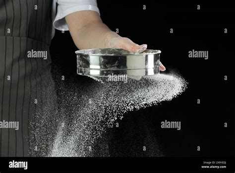 Woman Sieving Flour At Table Against Black Background Closeup Stock