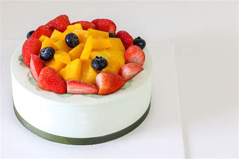 신선한 딸기 블루 베리 및 망고로 가득 찬 맛있는 과일 생일 케이크가 프레임과 흰색 테이블 왼쪽에 있습니다 0명에 대한 스톡