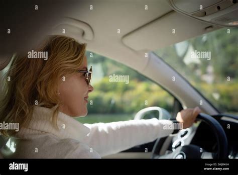A Blonde Woman In A White Sweater And Jeans Is Driving Happy Woman Sitting In A Car With A