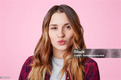 사랑 스러운 여성 모델의 잘생긴 남자와 Flirts로 입술 라운드 카메라 착용 체크 무늬 셔츠 외모는 긴 스트레이트 머리 핑크 배경 위에 절연 얼굴 표정 개념 귀여운에 대한
