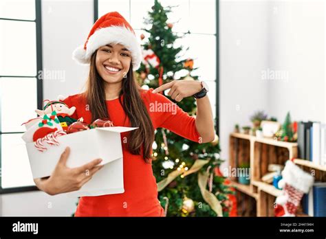 Junge Brünette Frau am weihnachtsbaum steht und Dekoration hält sieht selbstbewusst mit