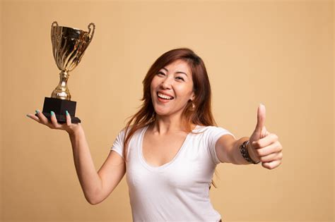 성공적인 젊은 아시아 여 자가 트로피를 들고 엄지손가락을 위로 표시 합니다 경쟁에 대한 스톡 사진 및 기타 이미지 경쟁