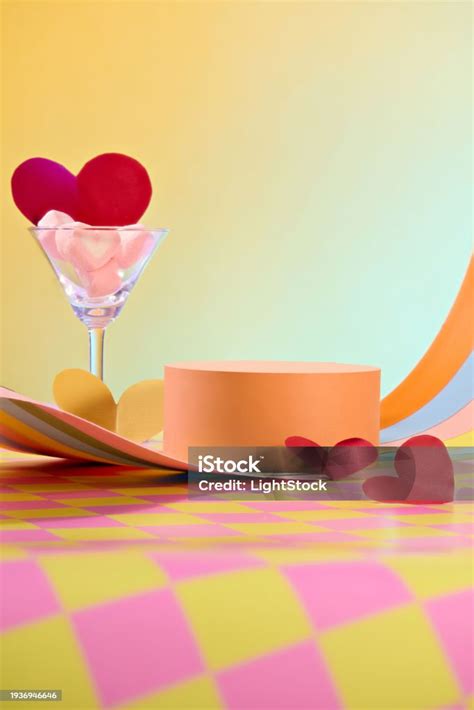 원통형 플랫폼은 프레임 중앙에 하트 모양의 마시멜로와 빨간색 종이 하트로 채워진 칵테일 잔 옆에 배치됩니다 바둑판 무늬 표면이 있는 그라데이션 배경입니다 강단에 대한 스톡