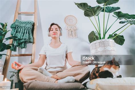 젊은 건강한 여자는 집에서 명상을 연습하고 헤드셋을 착용하고 현대적인 스칸디 인테리어 홈의 바닥 쿠션에 연꽃 자세로 앉아 있다 명상 휴식 눈 감고 선택적 초점 25 29세에
