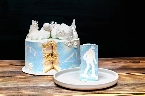 흰색 파란색 스폰지 맛있는 바닐라 크림 케이크는 큰 둥근 마시멜로 초콜릿 눈송이 전나무 산으로 잘라낸 조각 접시에 스키어 그림