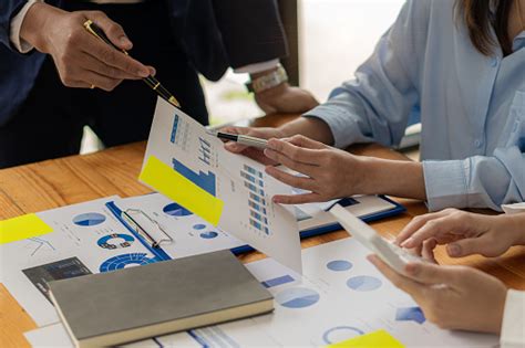 비즈니스 팀은 차트를 사용하여 프로젝트를 논의하고 계획하고 사무실 테이블에 펜과 분석 서류를 들고 있습니다 랩톱 컴퓨터와 백그라운드에서 실행되는 금융 그래프 비즈니스