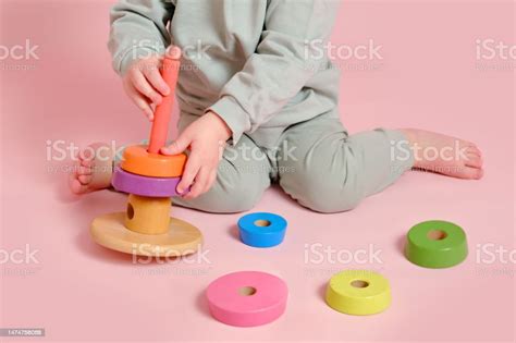 행복한 유아 아기는 스튜디오 분홍색 배경에 피라미드를 가지고 놀고 있습니다 어린 소년은 장난감 피라미드에 나무 반지를 끼웁니다 아이 나이 1 년 8 개월 보육에 대한 스톡