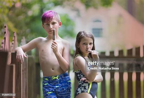 Brother And Sister Wearing Swimsuits Eating Popsicles In A Backyard