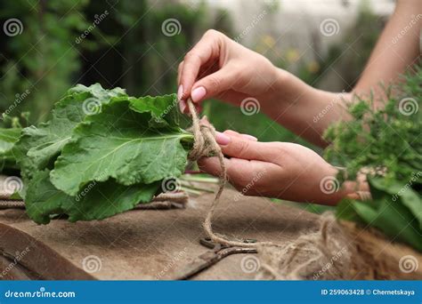 Woman Tying Bunch Of Fresh Green Leaves With Twine At Wooden Table Outdoors Closeup Drying