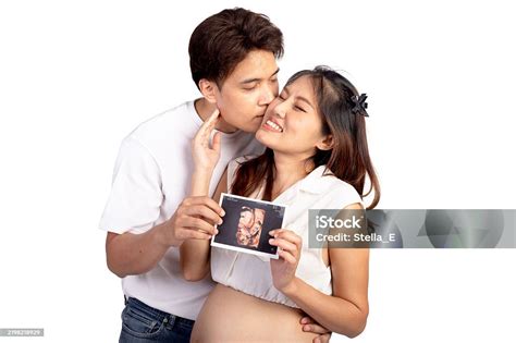 흰색 배경에 행복한 가족 아시아 커플 초음파 아기 아기 사진을 들고 아름다운 아내에게 키스하는 아시아 남편 큰 배를 가진 아름다운 미소 짓는 임산부 엄마 2명에 대한 스톡