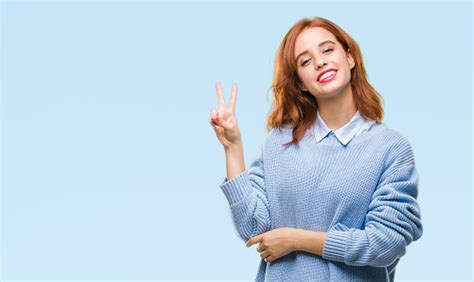격리 된 배경 승리 표시를 하 고 카메라에 윙크 하는 행복 한 얼굴로 웃 고 겨울 스웨터를 입고 위에 젊은 아름 다운 여자 번호