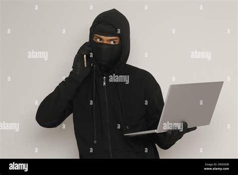 Portrait Of Mysterious Man Wearing Black Hoodie And Mask Doing Hacking Activity On Laptop