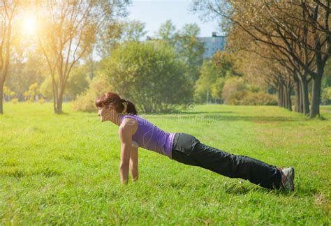 Smiling Sporty Woman Doing Fitness Plank Exercises Outdoor On The Grass