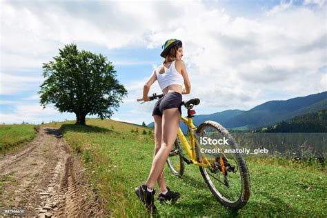 매력적인 여성 자전거 타는 사람 산에서 시골 길에 노란색 자전거를 타고 헬멧을 착용의 넓은 각도 보기 큰 나무 고 배경에 흐린 하늘입니다 야외 스포츠 활동 건강한 생활방식에