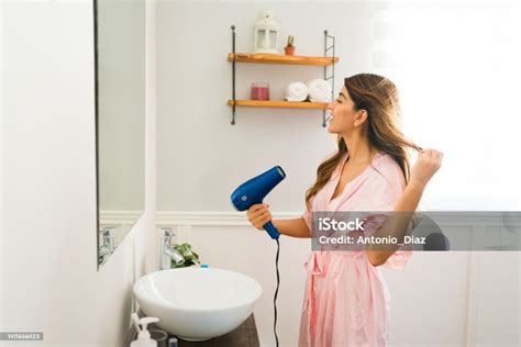 Side View Of An Hispanic Woman Blow Drying Her Hair After Showering