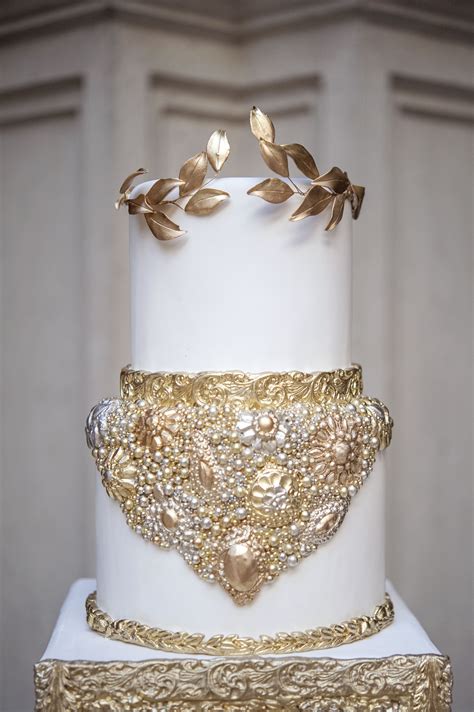 A White And Gold Wedding Cake With Leaves On Top