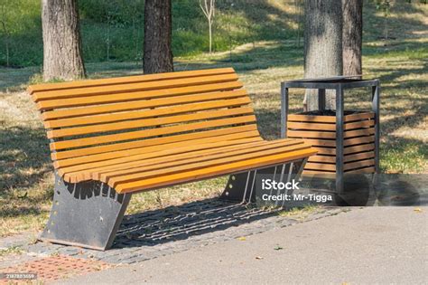 이미지는 두 개의 나무 벤치가 있는 공원 풍경을 묘사하며 하나는 수평 칸막이가 있고 다른 하나는 수직 칸막이가 있는 더 작은 나무 벤치가 있습니다 붉은 벽돌 포장재에 흩어져