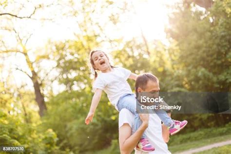 매력적인 젊은 남자는 자연에 그의 딸과 함께 재생 됩니다 아버지는 서 고 그의 뒤에 여자를 들고 그 옆으로 팔을 스트레칭입니다 가족은 웃 2명에 대한 스톡 사진 및 기타