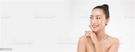 깨끗하고 신선한 피부 행복과 흰색 배경에 고립 된 긍정적 인 감정으로 쾌활한 부드러운 뺨 미소를 만지는 아름다운 아시아 여성의