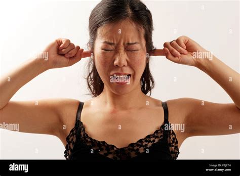 Young Asian Woman With Her Fingers In Her Ears To Protect Them From
