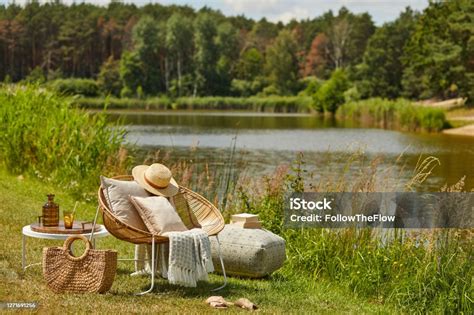 디자인 등나무 안락의자 커피 테이블 격자 무늬 베개 음료 및 우아한 액세서리와 호수에 야외 정원의 세련된 구성 여름 철꺼무 0명에 대한 스톡 사진 및 기타 이미지 Istock