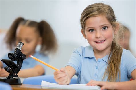귀여운 어린 소녀는 Stem 초등학교에서 현미경을 사용하여 수업 중에 답변을 씁니다 Stem 주제에 대한 스톡 사진 및 기타