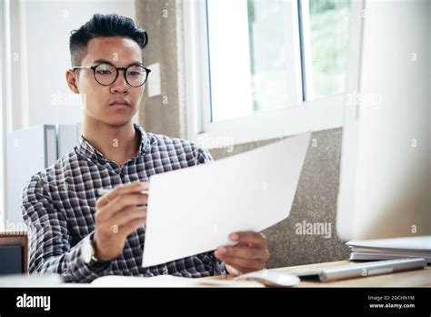 Pensive Young Entrepreneur In Glasses Proofreading Document And