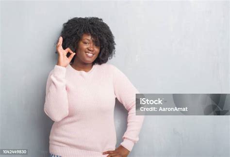 젊은 아프리카계 미국인 플러스 크기 여자 회색 그런 지 벽 입고 겨울 스웨터 웃 고 긍정적인 손과 손가락으로 Ok 사인을 하 고 이상 성공적인 식입니다 가을에 대한 스톡