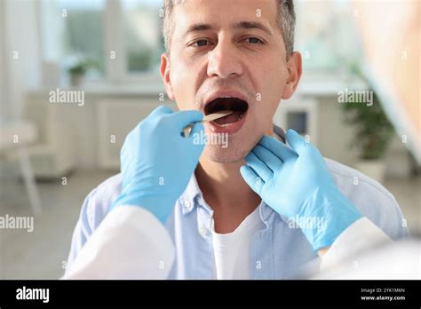 Doctor Examining Mans Throat With Tongue Depressor In Clinic Stock