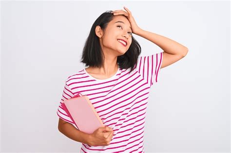 고립 된 흰색 배경 위에 서있는 책을 들고있는 젊은 아름다운 중국 여성은 부끄러움과 깜짝 얼굴에 충격을 받고 분노와 좌절에