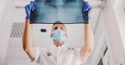 안면 마스크와 고무장갑을 낀 의사가 병원에 서서 코로나 바이러스 동안 폐의 엑스레이를 보고 있다 사진 Unsplash의 병원 이미지