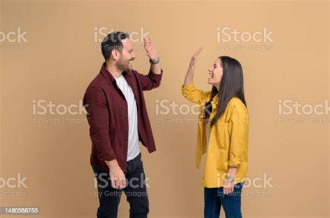 황홀한 남자와 여자는 성공을 축하하면서 비명을 지르고 서로에게 하이파이브를 합니다 흥분한 젊은 부부는 노란 배경 위에 서서