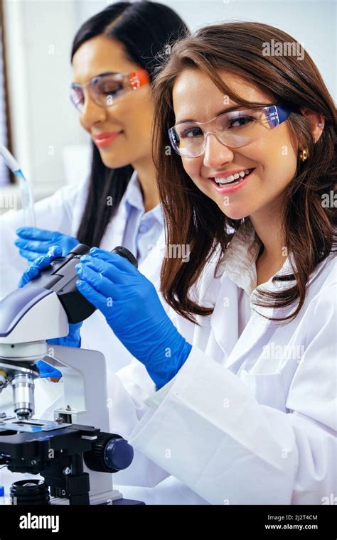 Young Female Scientist Using Microscope While Her Colleague Working In