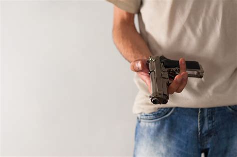 젊은 남자는 텍스트 복사 공간 흰색 벽의 배경에 손에 광택 금속 총을 보유 하고있다 보안 개념 강철에 대한 스톡 사진 및 기타