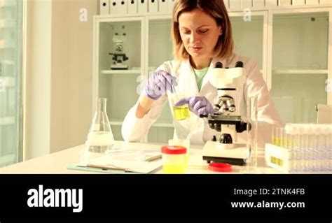 Female Lab Worker Stirs Patient Urine Sample In Jar Before Pouring Into Test Tube Concentrated