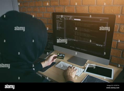 Hacker In The Hood Working With Computer And Holding Credit Card With