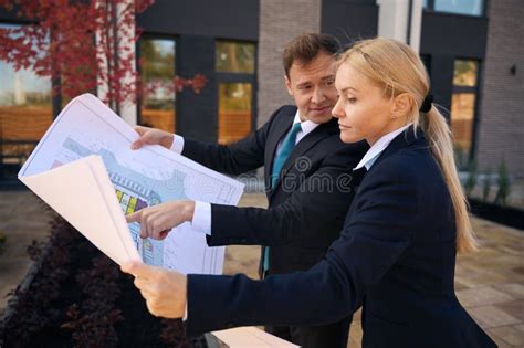 engineer and client standing near house with plan in hands stock image