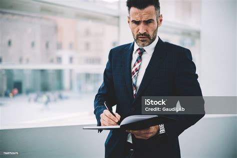 메모장에 정보 데이터를 쓰면서 카메라를 보고 자신감 있는 사업가 50 세의 절반 길이 초상화 본격적인 성공 자랑 Ceo 정장 입고 노트북에 메모를 만들기 50 54세에 대한