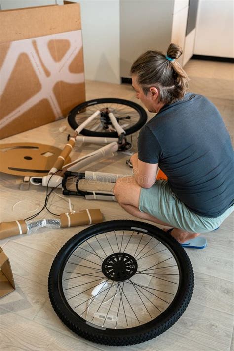 A Man Is Indoors Assembling A Bicycle In His Home Surrounded By Tools