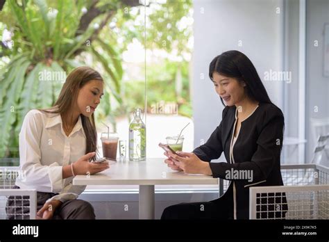 Two Asian Women Having A Pleasant Conversation Over Coffee In A Modern