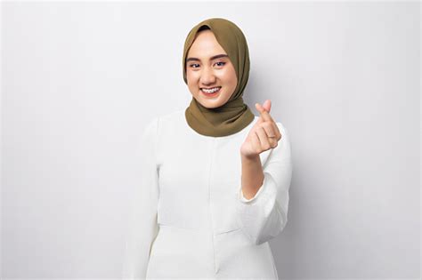 히잡을 쓰고 손가락 교차를 하고 흰색 배경에 고립된 카메라에 한국의 사랑의 표시를 보여주는 아름다운 미소 짓는 친절한 젊은