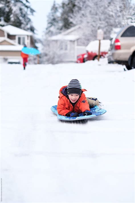 Asian Boy Sledding On The Street Outside Their Home By Stocksy