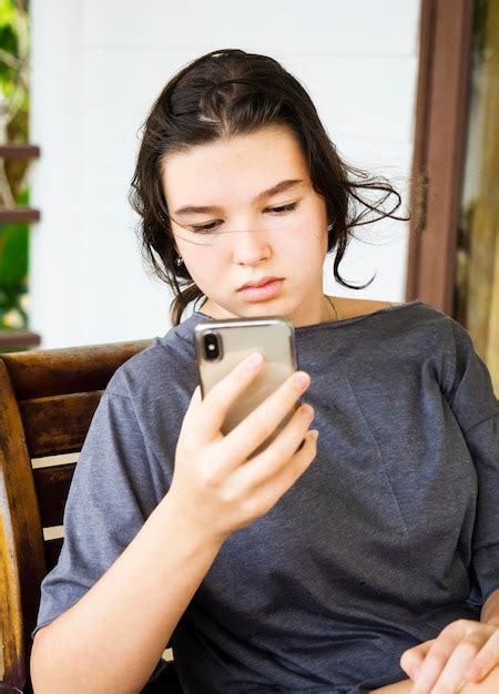 Close Up Of Girl Using Mobile Phone While Sitting On Chair Against Wall